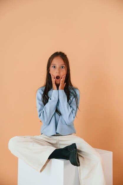 Premium Photo Shocked Cute Young Girl Is Sitting On White Cube In The