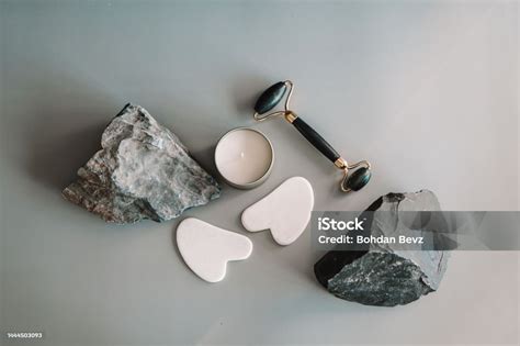 회색 배경에 옥 페이셜 롤러와 괄사 스크레이퍼와 천연석 자연석으로 만든 리프팅 테라피를위한 얼굴 마사지 세트 플랫 레이 탑 뷰 촛불 조명 장비에 대한 스톡 사진 및 기타