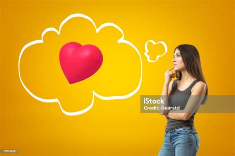 젊은 생각 갈색 머리 소녀 캐주얼 청바지와 노란색 배경에 빨간 마음과 티셔츠를 입고 광고에 대한 스톡 사진 및 기타 이미지