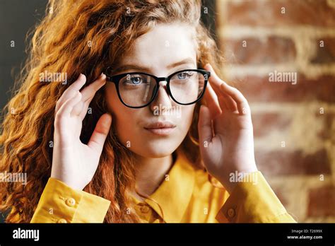 Curly Redhead Girl In The Yellow Shirt Wearing Spectacles Holding Hands Near Her Face While