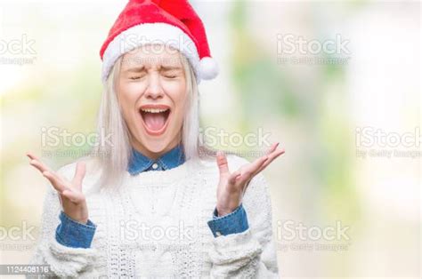 젊은 금발 여 자가 이상 크리스마스 모자를 쓰고 배경 축 제기 및 닫힌 눈 비명 흥분 하는 무기와 성공을 위해 미친 미친 하 고립 우승자 개념 겨울에 대한 스톡 사진 및
