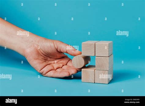 A Man Is Putting A Cylindrical Building Block In A Stack Of Rectangular Building Blocks On A