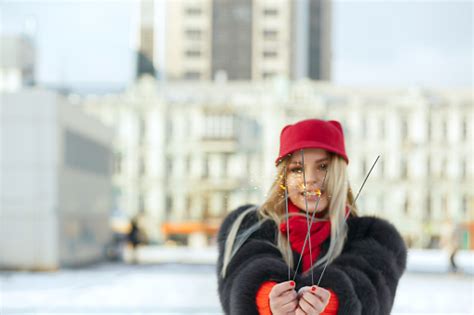 거리에서 스파클러와 함께 크리스마스를 축하하는 세련된 빨간 모자와 스카프를 입은 귀여운 금발 여성 텍스트 공간 20 24세에