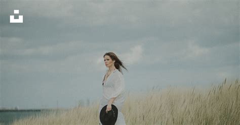 흰색 긴 소매 셔츠와 검은 바지를 입은 여자는 회색 아래 푸른 잔디밭에 서 있다 사진 Unsplash의 무료 바닷가 이미지