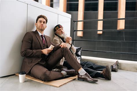 양복을 입고 넥타이를 맨 수심에 찬 사업가가 노인 노숙자와 함께 도시 거리에 앉아 연민과 사회적 책임을 보여주는 샌드위치를 나눠