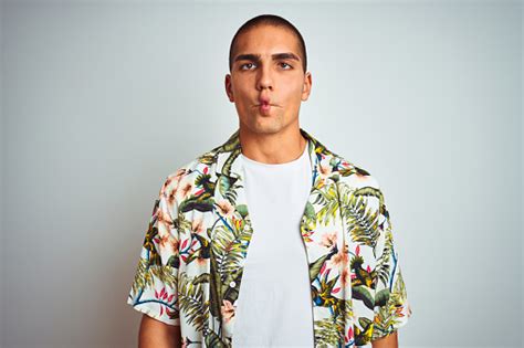 휴일에 젊은 잘생긴 남자는 입술 미친 코믹 제스처와 물고기 얼굴을 만드는 흰색 배경 위에 하와이 셔츠를 입고 재미있는 표현