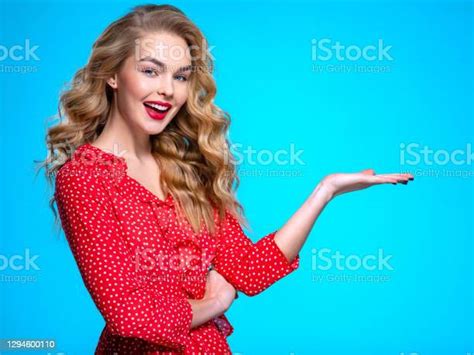 긍정적 인 감정을 가진 젊은 금발 의 여자 스튜디오에서 긴 흰 머리를 가진 아름다운 표현 소녀 빨간 셔츠에 감성 모델 행복한 흥분 백인 여성은 손바닥에 뭔가를 보여줍니다