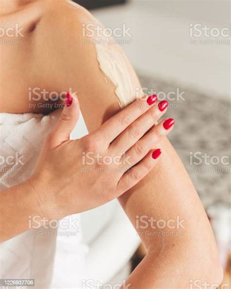 목욕이나 샤워 후 욕실에서 팔에 바디 크림이나 로션을 적용하는 수건에 빨간 손톱을 가진 아름다운 젊은 백인 여성 가정 생활에 대한 스톡 사진 및 기타 이미지 Istock