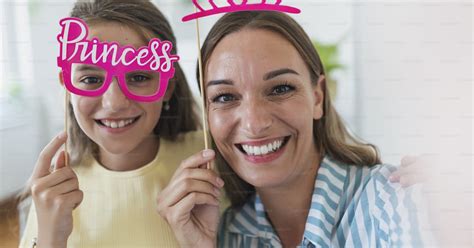 밝은 벽의 배경에 재미 있는 가족 어머니와 그녀의 딸 소녀가 종이 액세서리를 가지고 있다 엄마와 아이는 막대기에 종이 왕관을