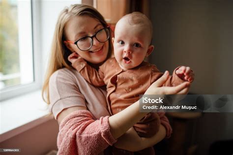 집에서 아늑한 방에서 창문 근처에 서있는 동안 잠옷을 입고 사랑스러운 아기를 들어 올리는 기쁘게 생각합니다 30 34세에 대한 스톡 사진 및 기타 이미지 Istock