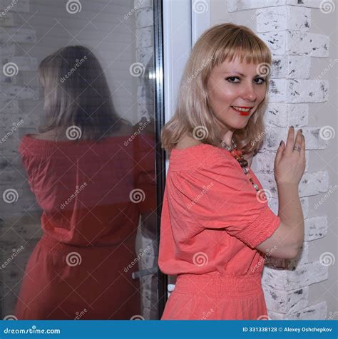Portrait Of Beautiful Blonde Girl In Coral Dress Posing At The Mirror