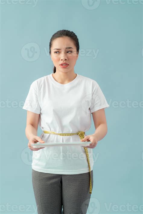 A Asian Woman Holding Scales With A Tape Measure Around Her Belly On A