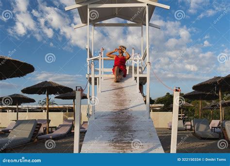Lifeguard Girl In A Red Dress On An Observation Tower On The Beach In