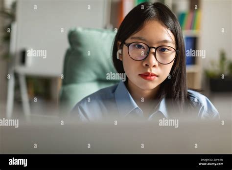 Japanese Business Female Wearing Earbuds Using Computer At Workplace