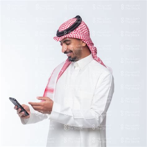 ذا ستوك رجل سعودي يرتدي الزي السعودي ويستعمل الجوال مع خلفية بيضاء