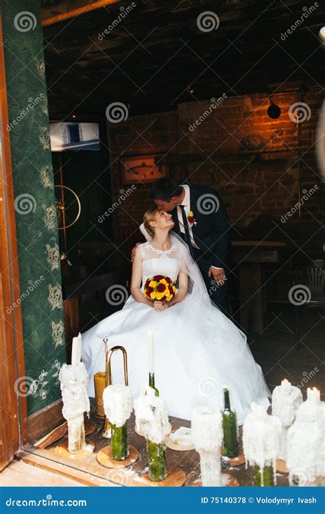 La Novia Se Sienta En Una Silla En Un Restaurante Viejo Mientras Que El Novio Lo Besa Foto De