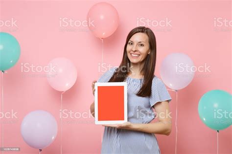 다채로운 공기 풍선 파스텔 핑크 배경에 빈 빈 화면 태블릿 Pc 컴퓨터를 들고 파란 드레스를 입고 웃는 매력적인 젊은 여자의 초상화 생일 휴가 파티 개념 14에 대한 스톡
