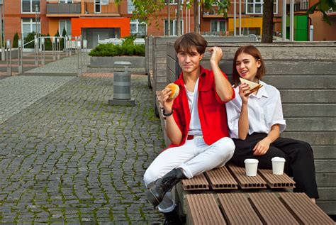 함께 야외에서 점심을 먹는 남자와 여자 햄버거와 샌드위치를 먹는 커플 패스트 푸드와 길거리 음식의 개념 종이 용기와 일회용 컵의