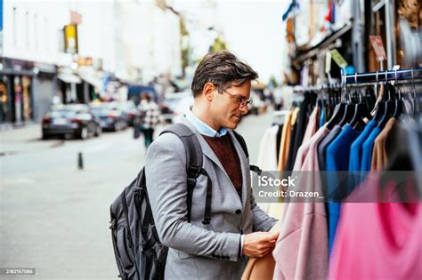 안경을 쓰고 배낭을 멘 남자가 밝은 날에 자동차와 사람들로 가득 찬 도시 거리에서 옷을 쇼핑하고 있습니다 35 39세에 대한 스톡 사진 및 기타 이미지 Istock