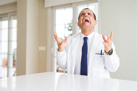 중년의 의사는 병원에서 의료 코트를 입고 미친 미친 소리와 공격적인 표정과 팔을 들고 고함쳤다 좌절 개념입니다 감정에 대한 스톡