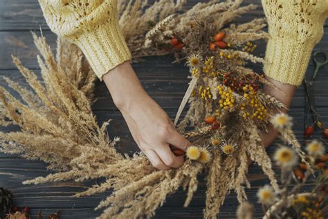 세련된 가을 화환 만들기 마른 풀 야생화 밀을 들고 나무 테이블에 소박한 화환을 만드는 손 가을 휴가 워크샵 어두운