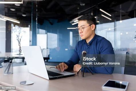 사무실 내부 직장에서 온라인 비즈니스 과정을 녹음하는 진지한 교사 온라인으로 학생들을 가르치는 노트북을 가진 아시아 남자 캐주얼 셔츠를 입은 사업가 멀리 떨어진에 대한 스톡