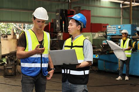 보호복을 입은 기술자 엔지니어 또는 작업자가 중공업 제조 공장에서 금속 기계를 제어하거나 유지 보수하는 동안 서서 워키토키 라디오를 사용하는 작업자 30 34세에 대한 스톡