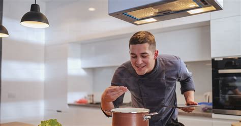 제복을 입은 헌신적인 백인 요리사가 태블릿을 들고 스토브 옆에 서서 부엌에 서서 끓는 식사 냄새를 맡고 있다 사진