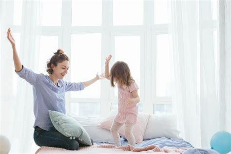 젊은 어머니과 그녀의 작은 딸 재생와 쿠션에 침대 재미 있는 베개 싸움 부드러운 파스텔 색상 분홍색과 파란색 선택적 초점 함께 플레이 하 고 순간을 즐기세요 주말에 가족