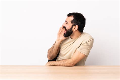 Premium Photo Caucasian Man With Beard In A Table Shouting With Mouth Wide Open To The Side