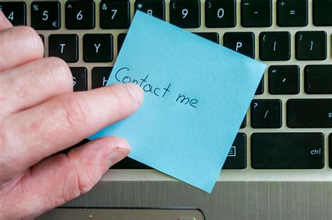 노트북 키보드에 Contact Me라고 적힌 스티커 메모를 붙이는 손으로 전문적인 환경에서 의사 소통과 알림을 상징합니다 개념에