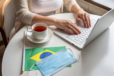 여자 관광객 은 노트북에서 일하는 커피 한 잔과 함께 아침 식사를합니다 브라질의 국기 카페의 테이블에 의료 보호 얼굴 마스크 공공 장소에서 박테리아와 바이러스로부터 보호