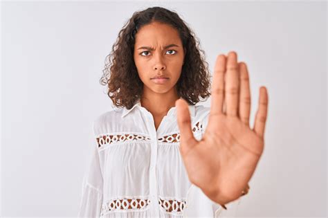 고리 된 흰색 배경 위에 서있는 셔츠를 입은 젊은 브라질 여성은 진지하고 자신감있는 표정 방어 제스처로 정지 표지판을 하고 있는 오픈 핸드로 서 있습니다 금지됨에 대한 스톡