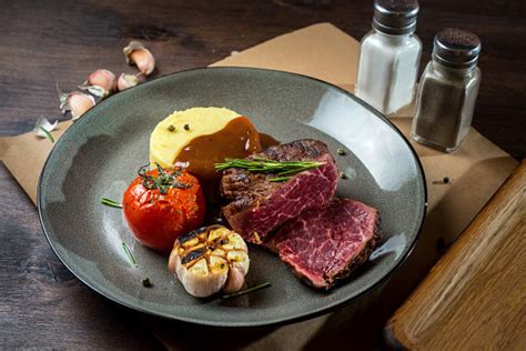 으깬 감자와 구운 토마토와 마늘을 로즈마리 스프릭이 든 접시에 담은 필렛 미뇽 드물게 튀김의 정도 육즙이 많은 쇠고기 안심 조각 0명에 대한 스톡 사진 및 기타 이미지