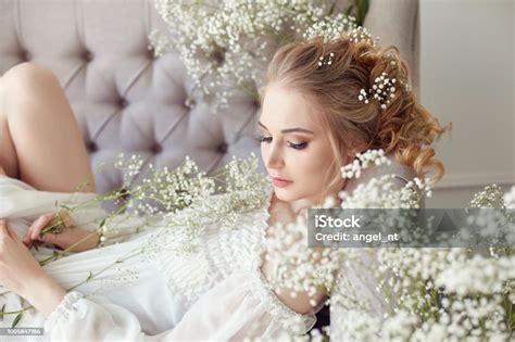 소녀 흰색 빛 드레스와 곱슬 머리 꽃 집에서 여자의 초상화 근처 창 순수성 및 순 결 곱슬 금발 로맨틱 봐 아름 다운 눈 손에