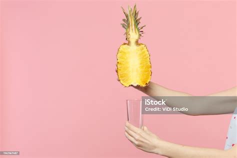 신선한 잘 익은 파인애플 과일 분홍색 파스텔 벽 배경에 고립 된 유리 컵의 절반의 손에 여자 홀드의 자른 사진을 닫습니다 사람들은 생생한 라이프 스타일 휴식 휴가 개념입니다
