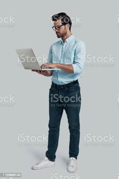 인터넷 서핑 회색 배경에 서 있는 동안 노트북을 사용 하 여 젊은 남자의 전체 길이 전신에 대한 스톡 사진 및 기타 이미지