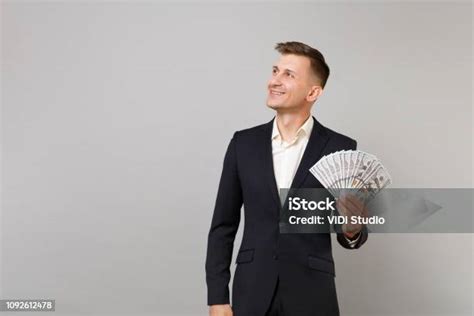 옆으로 달러 지폐 현금 돈 회색 배경에 고립의 많은 무리를 들고 검은 양복에 웃는 젊은 비즈니스 사람 성과 경력 부 비즈니스 개념입니다 복사 공간을 비웃는 다 검은색에 대한