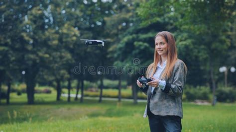 Businesswoman Piloting A Drone Using A Remote Controller In A City Park Enjoying A New