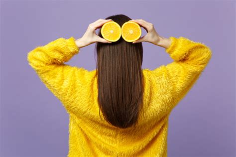 보라색 파스텔 배경에 고립 된 머리 근처 신선한 잘 익은 오렌지 과일의 Halfs를 들고 모피 스웨터에 젊은 여자의 뒷 전망 사람들은 생생한 라이프 스타일 휴식 휴가