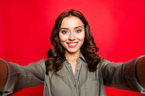 아주 꿈꾸는 듯한 매력적인 아름 다운 귀여운 달콤한 여자 타고 Selfie 현대 스마트폰 확인 흰색 할리우드 이빨 미소 밝은 빨간색 배경에 고립의 전면 카메라 갈색 머리에