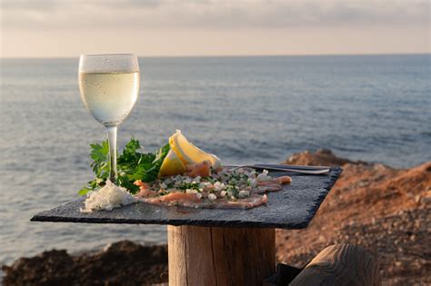 훈제 연어 필레 다진 흰 양파 잘 익은 레몬 셀러리 잔가지 와인 한 잔이 있는 검은 돌 테이블 바다 해안을 배경으로 해산물에 대한 스톡 사진 및 기타 이미지 Istock