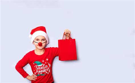 빨간 산타의 모자와 코를 쓴 귀여운 백인 아이 십대 소년이 디자인이나 텍스트를 위한 빈 복사 공간을 들고 있다 기치 크리스마스 모형 템플릿입니다 가방에 대한 스톡 사진 및