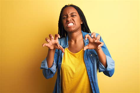 고양이 공격적이고 섹시한 표현으로 발톱 제스처를하고 재미 웃고 고립 된 노란색 배경 위에 서 데님 셔츠를 입고 젊은 아프리카 계