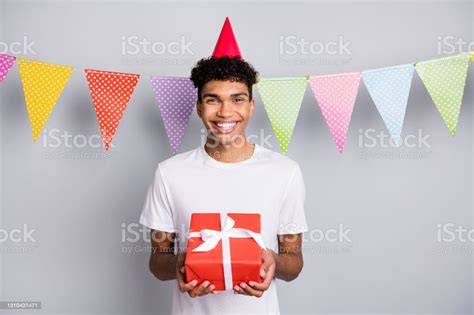 브루넷 낙관적 곱슬 좋은 남자의 초상화 는 회색 배경에 고립 된 흰색 티셔츠 모자를 착용 선물을 개최 T 셔츠에 대한 스톡 사진