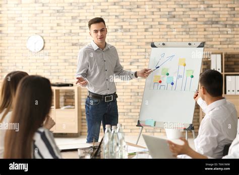 Young Man Giving Presentation During Business Meeting In Office Stock