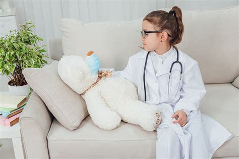의사 코트 청진기와 안경을 입고 소파에 앉아 아픈 테디 베어를 돌보는 예쁜 어린 소녀 검사 보기에 대한 스톡 사진 및 기타 이미지 검사 보기 아이 테디 베어 Istock