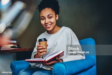 미소 아프리카 계 미국인 젊은 여자의 초상화 커피 컵 과 메모장 할 할 목록 의자에 앉아 행복 한 어두운 피부 여성 블로거 휴식 에 휴식 에 아늑한 인테리어 보고 카메라