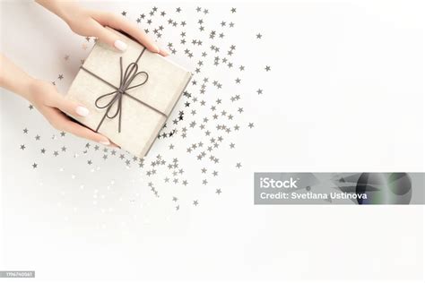 실버 스타 Sheped 반짝이 흰색 배경에 우아한 회색 활과 함께 현재 상자를 들고 아름 다운 흰색 매니큐어와 여성 손 휴일축제 배경 플랫 레이 스타일입니다 색종이 조각에