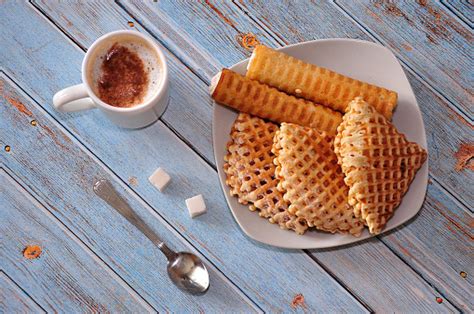 여러 가지 와플 숟가락 계피를 곁들인 신선한 카푸치노 한 잔을 곁들인 흰색 세라믹 접시가 나무 테이블에 서 있습니다 구이에 대한 스톡 사진 및 기타 이미지 Istock